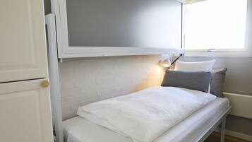 Quarto pequeno com uma cama de solteiro, dossel branco e janela com luz natural.