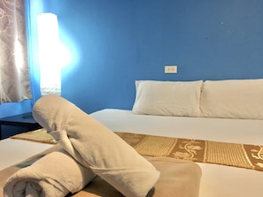 Quarto de hotel com cama, mesa de cabeceira, luminária e janela com cortinas.
