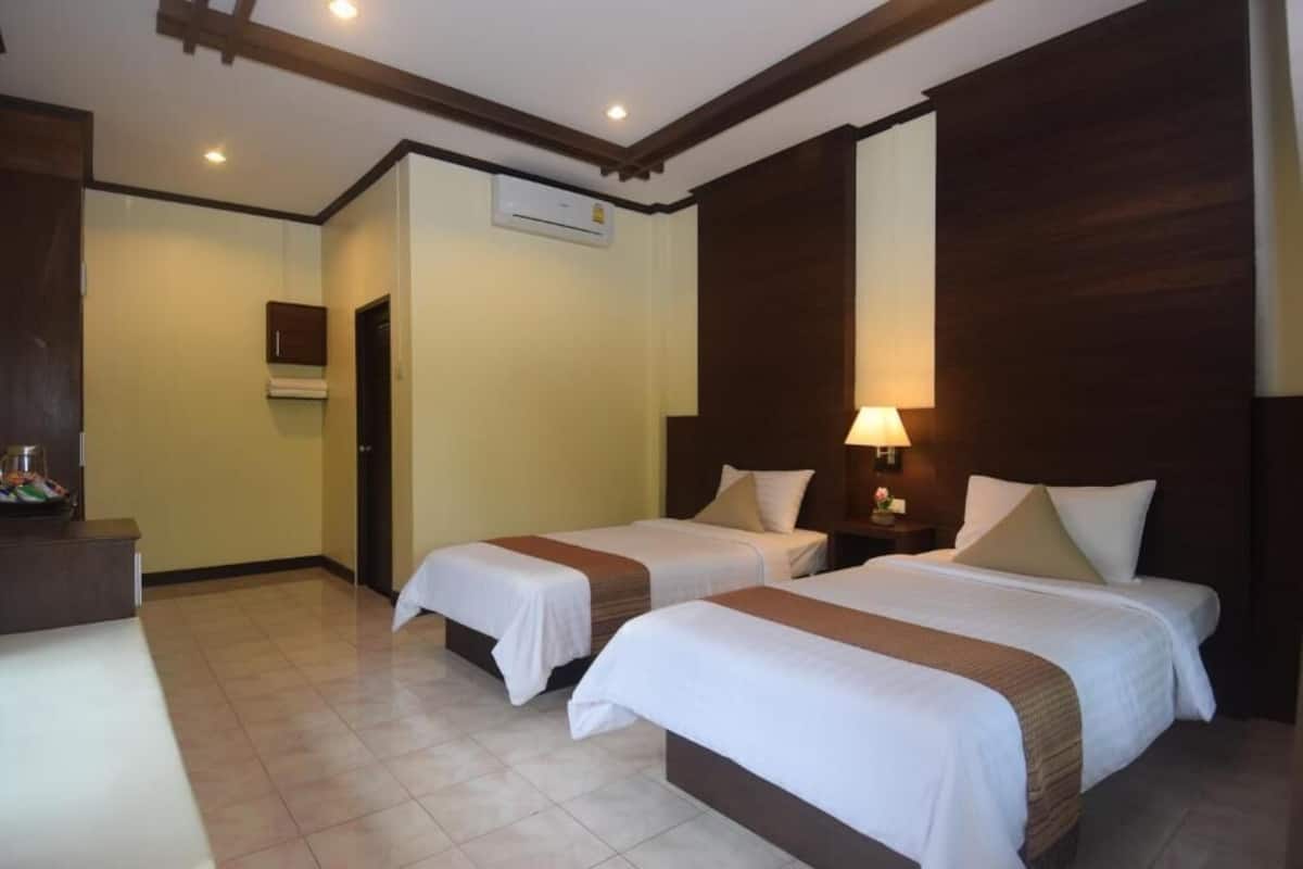 Quarto de hotel com duas camas de solteiro, uma escrivaninha, uma cadeira, mesa de cabeceira com luminária e ar condicionado na parede.
