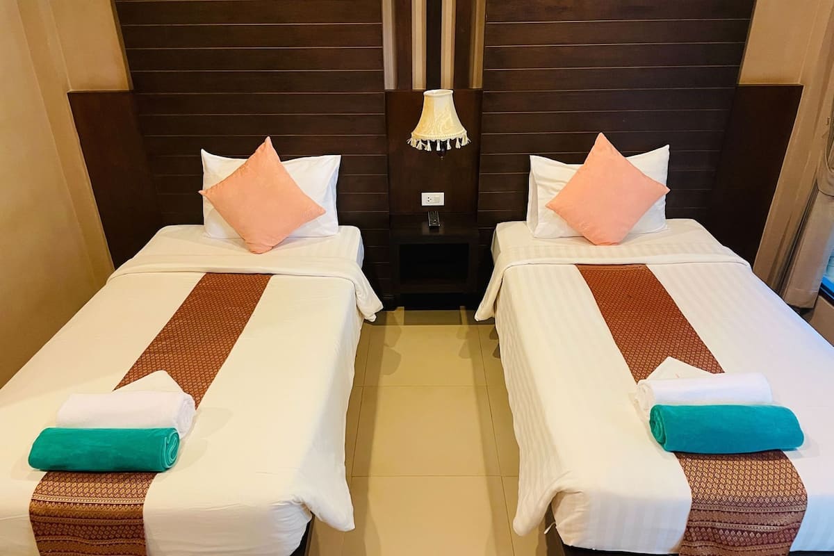 Duas camas de casal com roupa de cama branca, almofadas cor de pêssego e mantas decorativas castanhas.