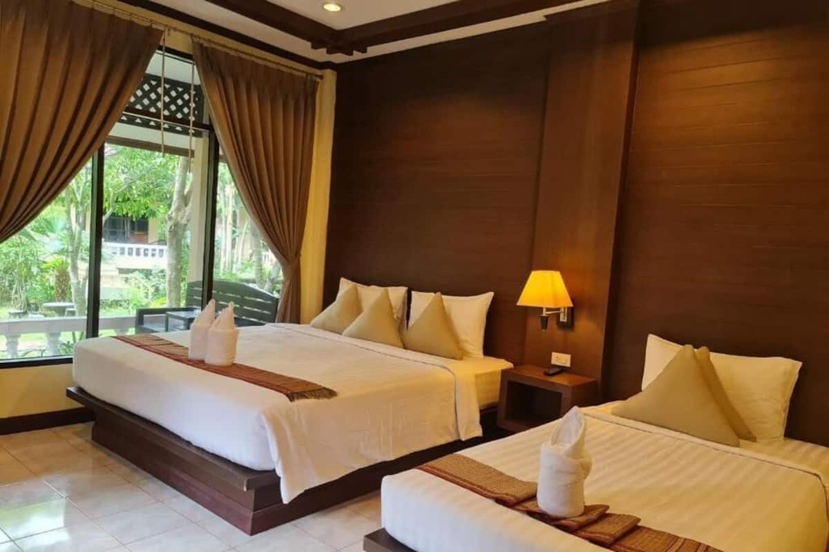 Quarto de hotel com duas camas, uma janela com cortinas, mesa de cabeceira com abajur e vista para o verde lá fora.