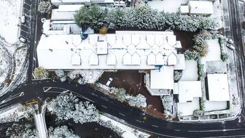 Vista aérea de um edifício com várias estruturas brancas, rodeado por estradas e árvores cobertas de neve.