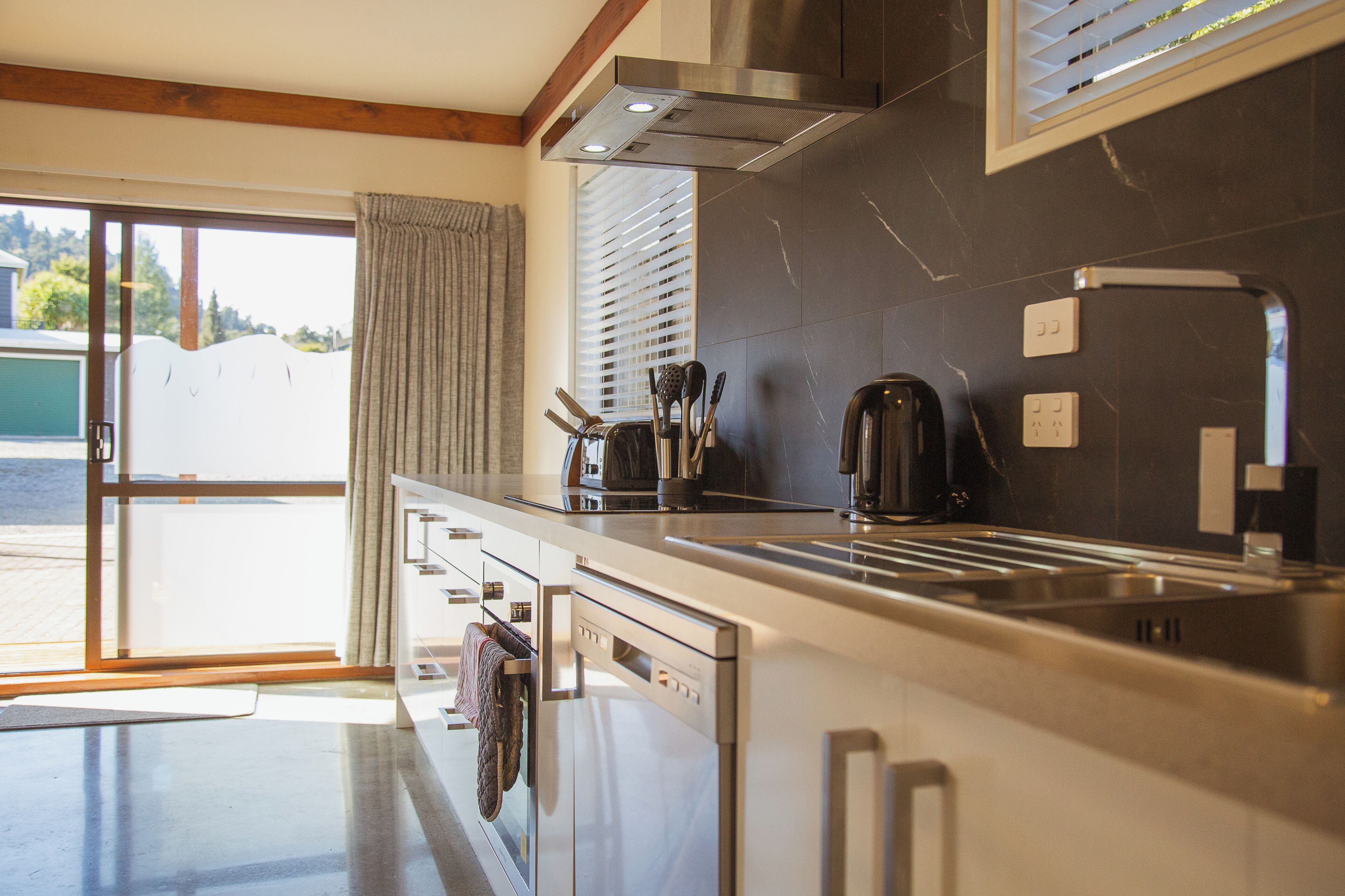 Uma cozinha moderna com bancada de aço inoxidável, forno embutido e janela com persianas.
