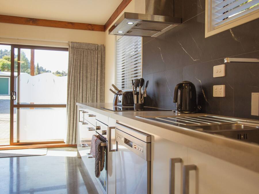 Uma cozinha moderna com bancada de aço inoxidável, forno embutido e janela com persianas.