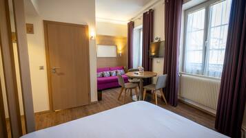Quarto de hotel com cama, sofá, mesa de jantar com cadeiras, televisão e janela com cortinas.
