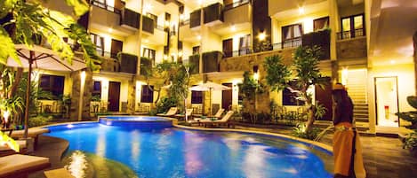 Uma piscina cercada por espreguiçadeiras e guarda-sóis, com um edifício de vários andares ao fundo.