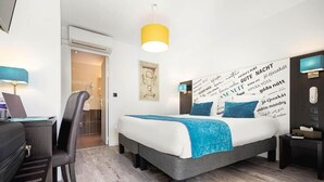Quarto de hotel moderno com cama, escrivaninha, cadeira e parede com texto.