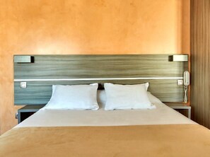Cama bem arrumada com cabeceira de madeira, dois travesseiros e mesa de cabeceira com um telefone.