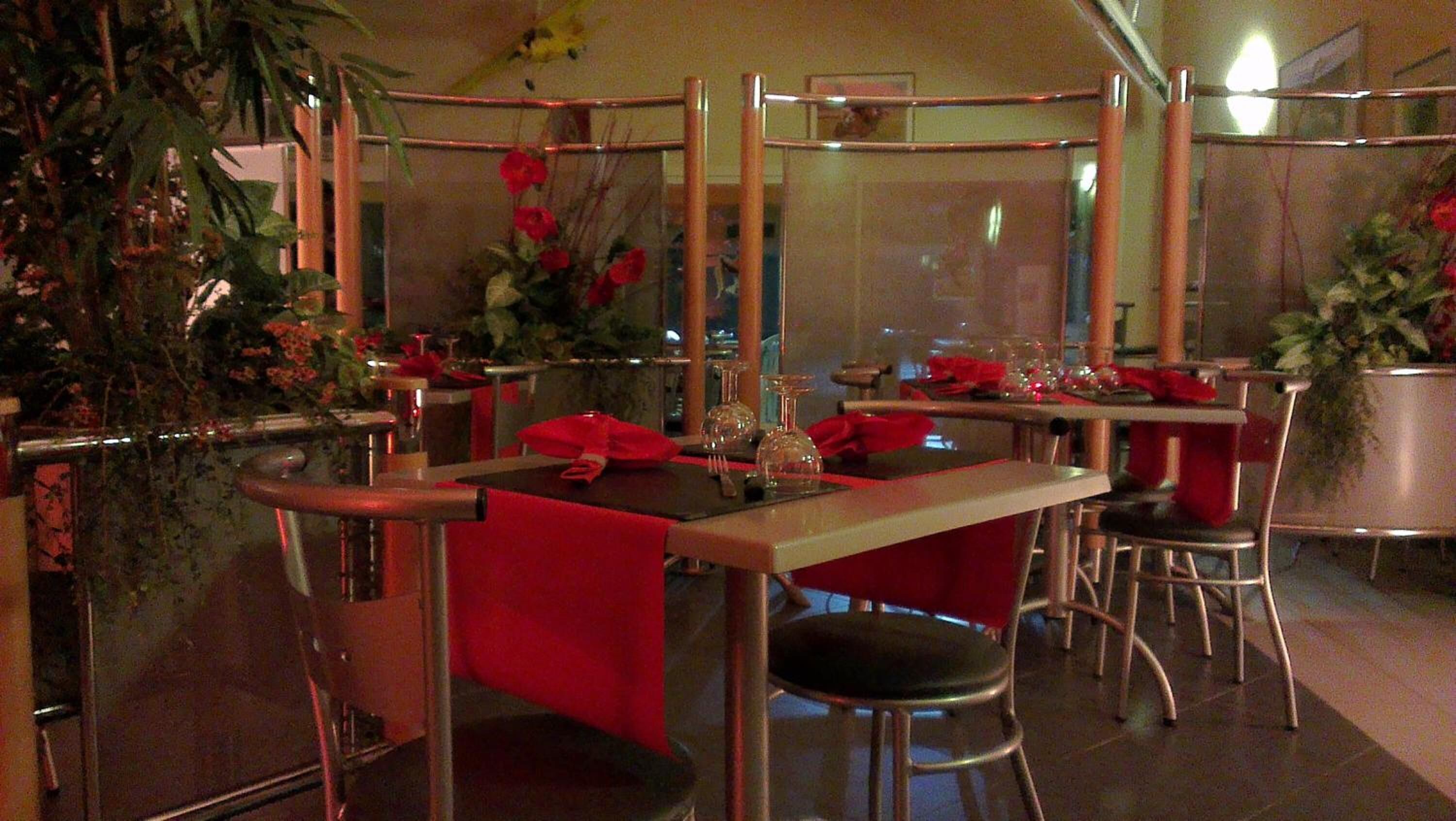 Um restaurante com interior moderno, destacando banquetas de metal, guardanapos vermelhos e plantas em vasos.
