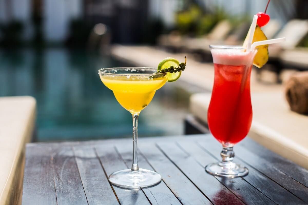 Dois cocktails numa mesa de madeira à beira da piscina.