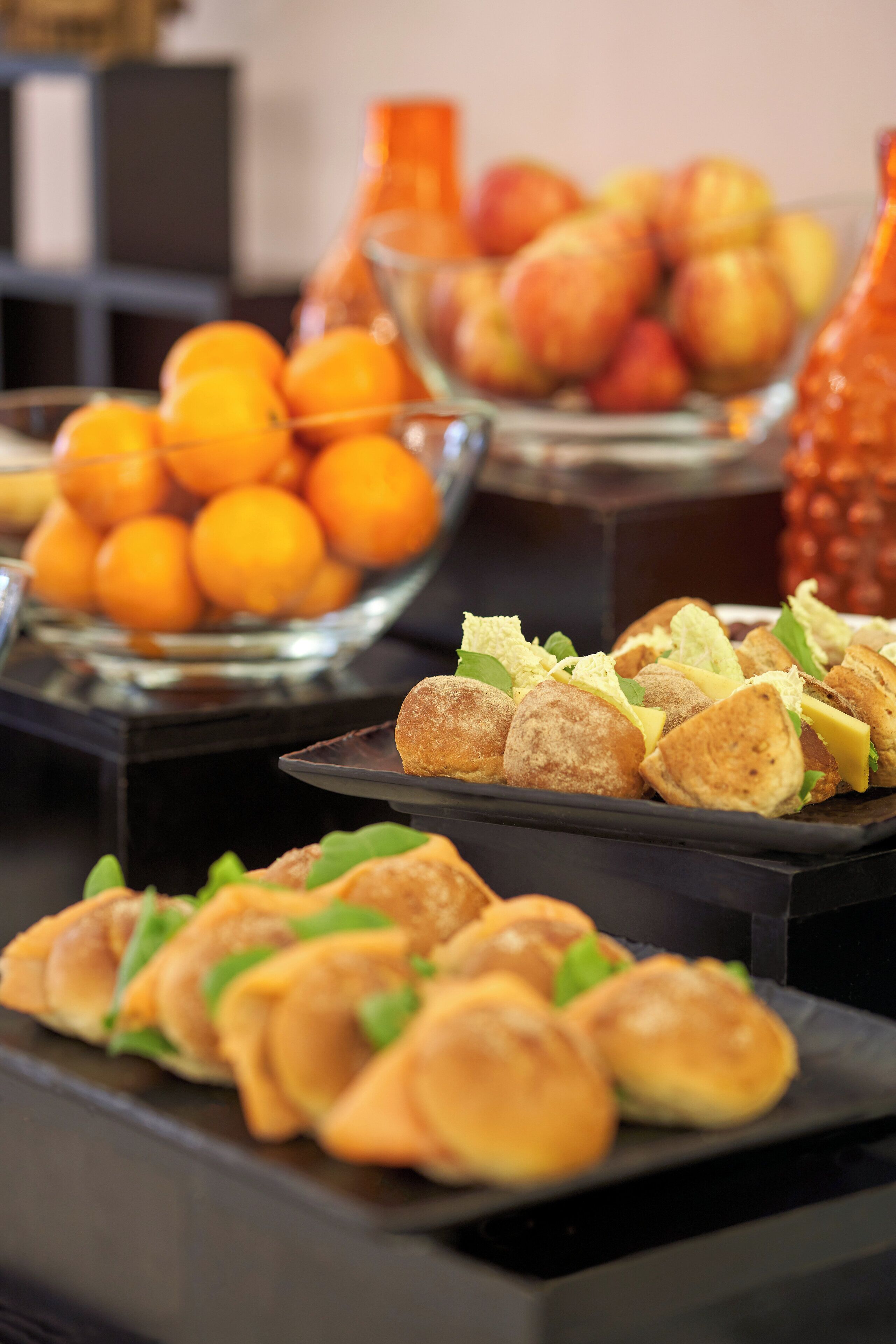 Buffet com diversos alimentos, incluindo laranjas, maçãs e doces.