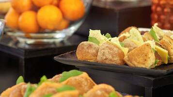 Buffet com diversos alimentos, incluindo laranjas, maçãs e doces.