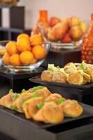 Buffet com diversos alimentos, incluindo laranjas, maçãs e doces.