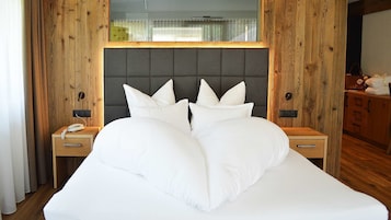 Uma cama grande com cabeceira estofada cinza, duas mesas de cabeceira com luminárias e um guarda-roupa de madeira.