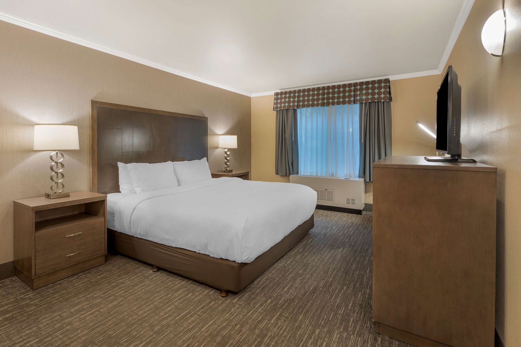 Quarto de hotel com cama, mesas de cabeceira, televisão, janela com cortinas e ar condicionado fixado na parede.