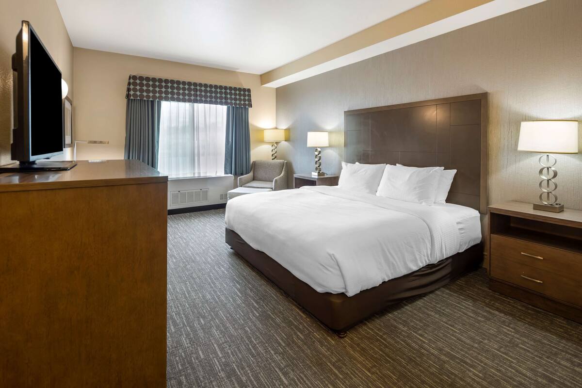 Quarto de hotel com uma cama grande, uma escrivaninha, uma cadeira, duas mesas de cabeceira com luminárias e uma televisão.