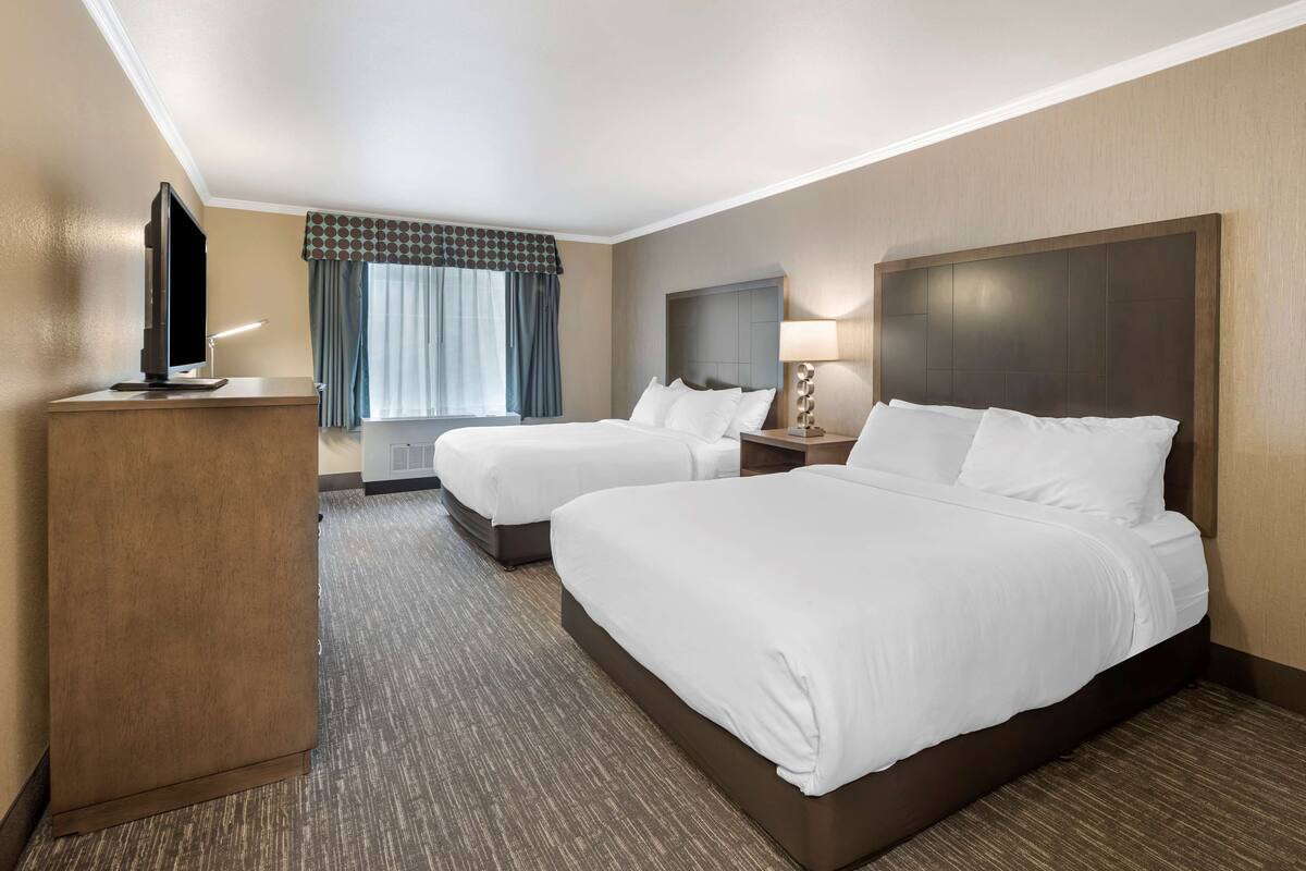 Quarto de hotel com duas camas, televisão, escrivaninha e janela com cortinas.