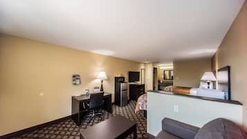 Quarto de hotel com escrivaninha, cadeira, sofá e uma pequena área de cozinha.