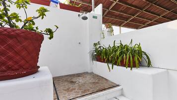 Uma pequena área externa com um cachepot vermelho, uma parede branca e uma estrutura de cobertura metálica.