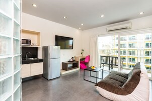 Um apartamento moderno com cozinha, sala de jantar e sala de estar. Possui uma televisão de tela plana, geladeira, mesa de jantar e um sofá.
