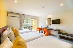 Quarto de hotel com duas camas, uma escrivaninha, uma cadeira, uma TV e varanda com vista para prédios.