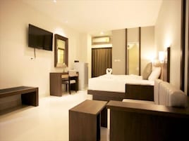 Quarto de hotel moderno com uma cama grande, uma escrivaninha, uma cadeira, uma televisão de tela plana na parede e um sofá.