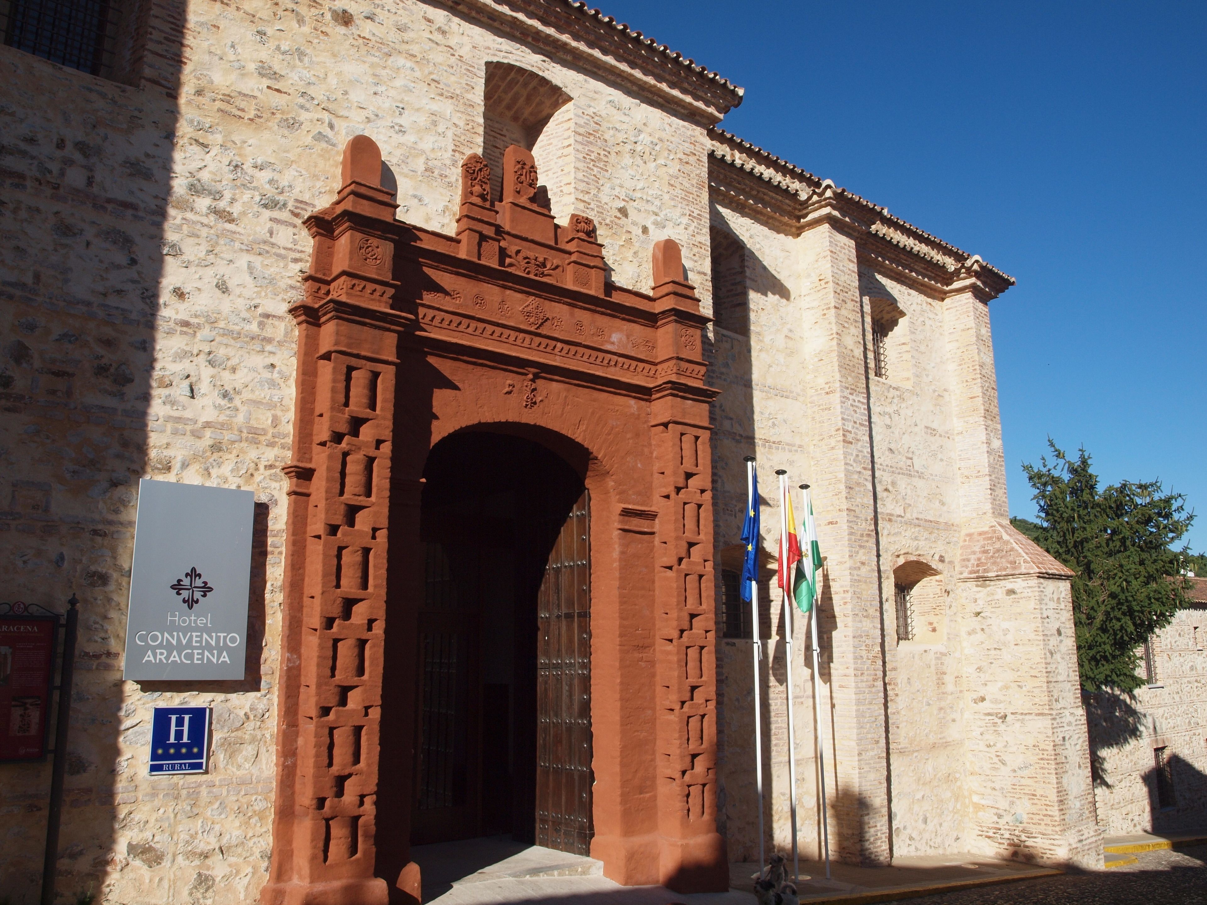 Um edifício histórico com uma entrada imponente em arco, bandeiras e uma placa indicando Hotel Convento Aracena.