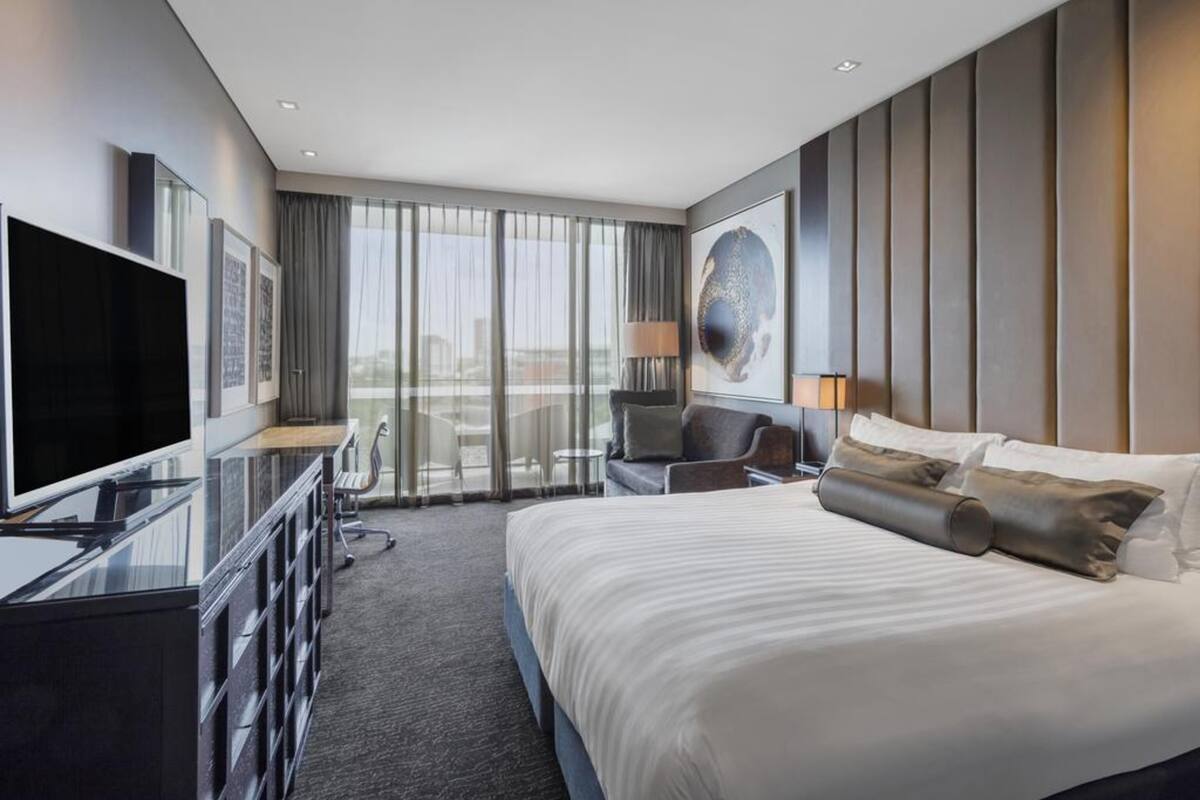 Quarto de hotel moderno com cama grande, escrivaninha, televisão de tela plana, sofá e uma grande janela com cortinas.