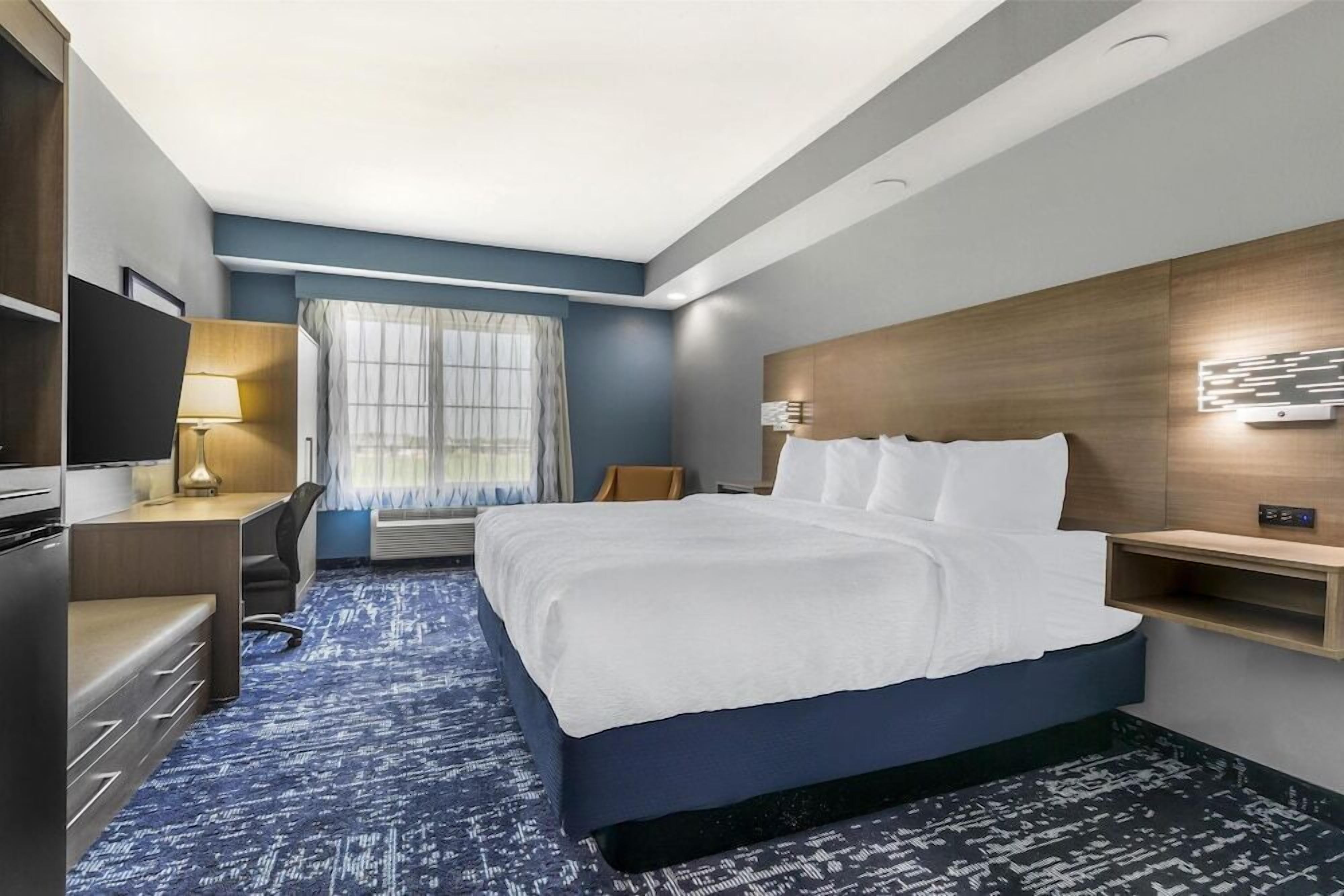 Quarto de hotel com cama, escrivaninha, cadeira, televisão e janela com cortinas.
