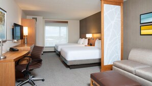Quarto de hotel com escrivaninha, duas camas, sofá e televisão.