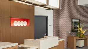 Uma área de recepção com painel de parede em madeira, uma porta escura e um balcão de recepção com detalhes em luz vermelha.