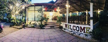 Um edifício com uma placa de 'WELCOME', uma entrada coberta e um calçadão pavimentado que leva à entrada.