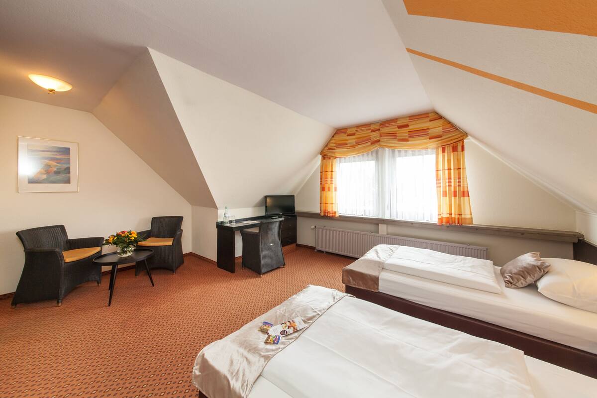 Quarto de hotel com duas camas, uma escrivaninha, uma cadeira e uma televisão.