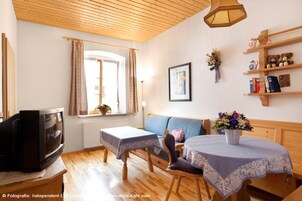 Uma sala de estar aconchegante com televisão, sofá, mesa pequena e uma janela com cortinas.