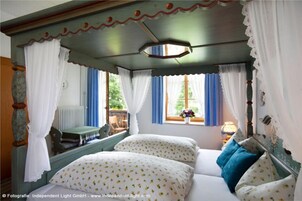 Quarto com cama de dossel, uma mesinha e janela com cortinas.