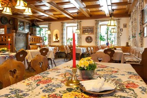 Restaurante com mobiliário de madeira, toalhas de mesa florais e um castiçal vermelho como peça central.