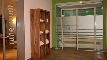 Uma área de recepção de hotel com um balcão de madeira, uma porta de vidro com a palavra "campf" e uma parede verde.