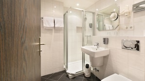 Casa de banho moderna com cabine de duche em vidro, lavatório branco e espelho com secador de cabelo.