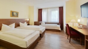 Quarto de hotel com duas camas de solteiro, uma escrivaninha, uma cadeira, uma televisão e uma janela com cortinas.