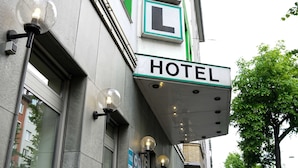 Um hotel com placa visível, iluminação externa e caixas de flores.