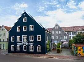 Hotel chamado 'Hotel Bergbauer', com fachada escura e imponente e diversas janelas.