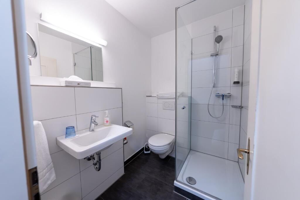 Uma casa de banho moderna com chuveiro em cabine de vidro, lavatório branco e sanita.