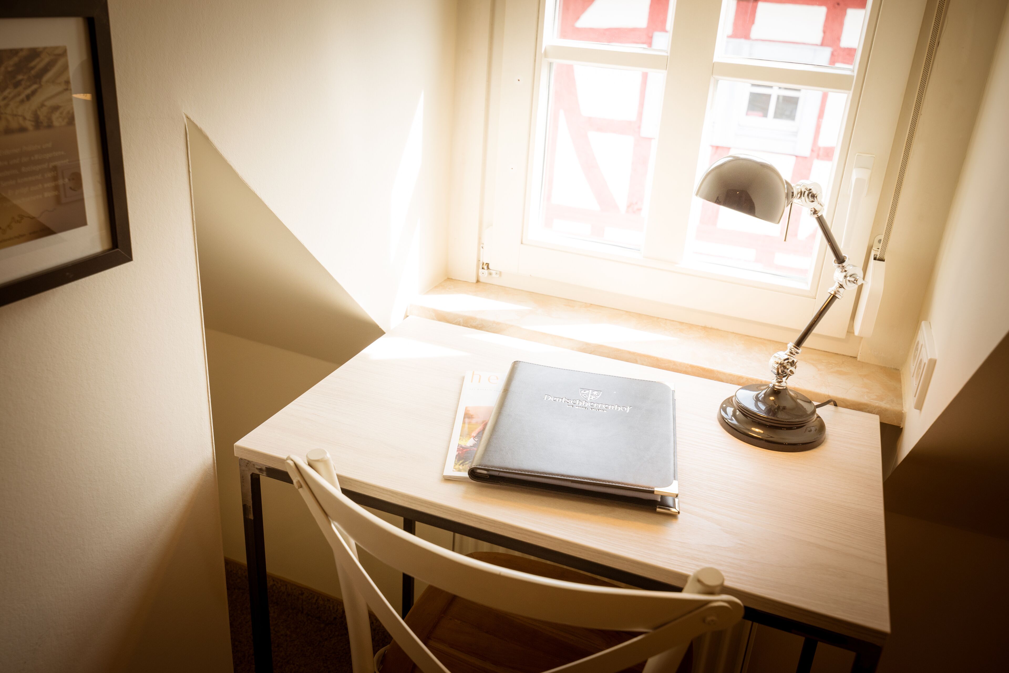 Uma pequena mesa com um laptop, uma luminária e um quadro na parede.