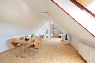 Um quarto moderno de conceito aberto, com teto inclinado, área de refeições com mesa e cadeiras, e vista para um quarto com cama e cômoda.