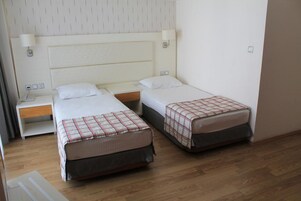 Quarto de hotel com duas camas de solteiro, piso de madeira e cabeceira branca.