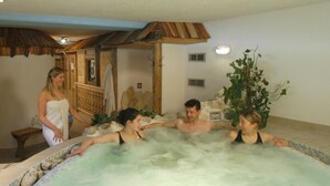 Uma banheira de hidromassagem com quatro pessoas, em ambiente rústico com vigas de madeira e parede de pedra.
