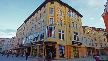Um edifício em esquina com uma placa 'HOTEL', várias lojas e uma área para pedestres.