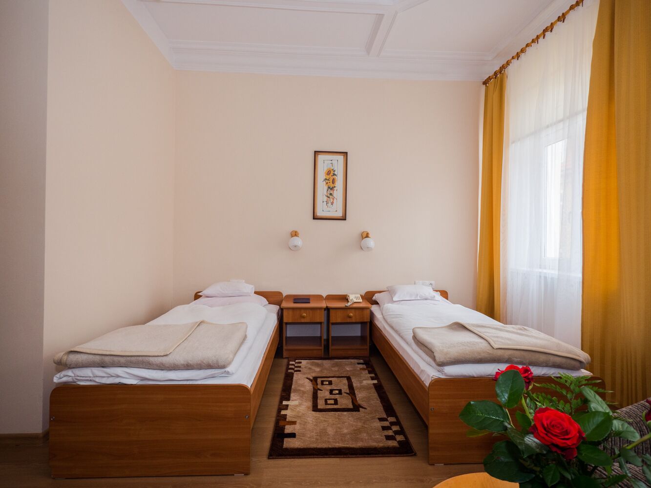 Quarto de hotel com duas camas de solteiro, uma mesinha com telefone e um tapete com padrão geométrico.