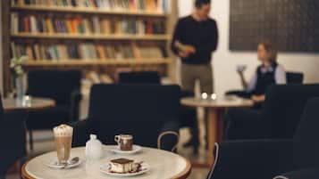 Um café acolhedor com mesas redondas, uma estante de livros e um muro com lousa.