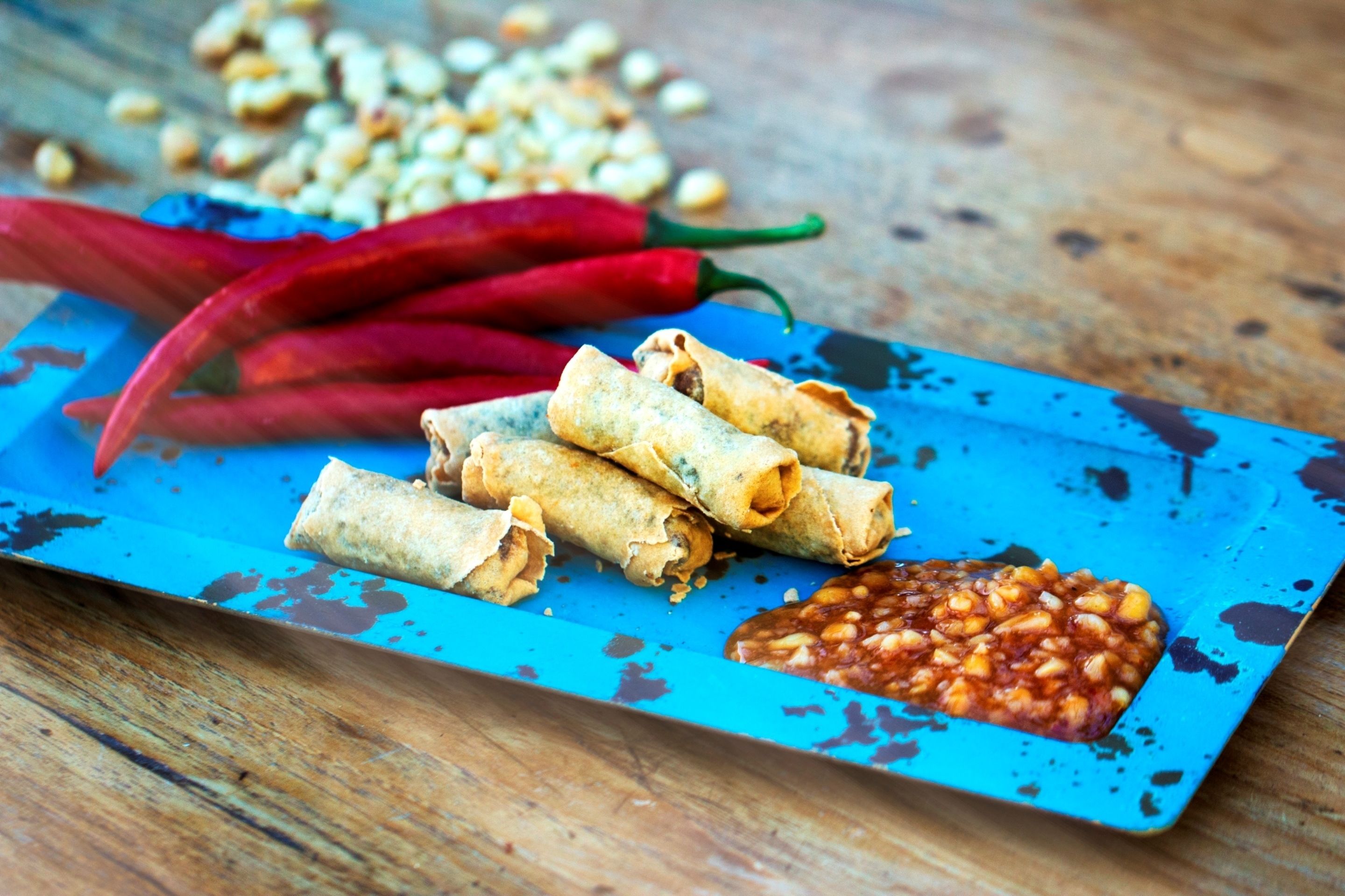 Um prato azul com salgadinhos fritos, pimentas vermelhas e molho de chili.